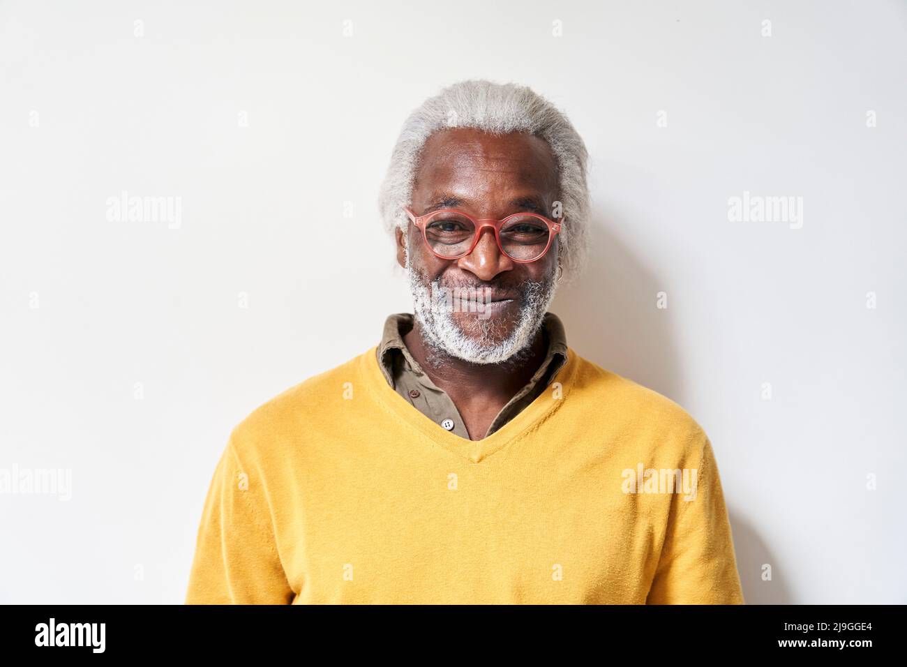 Smiling senior man standing against wall Stock Photo - Alamy