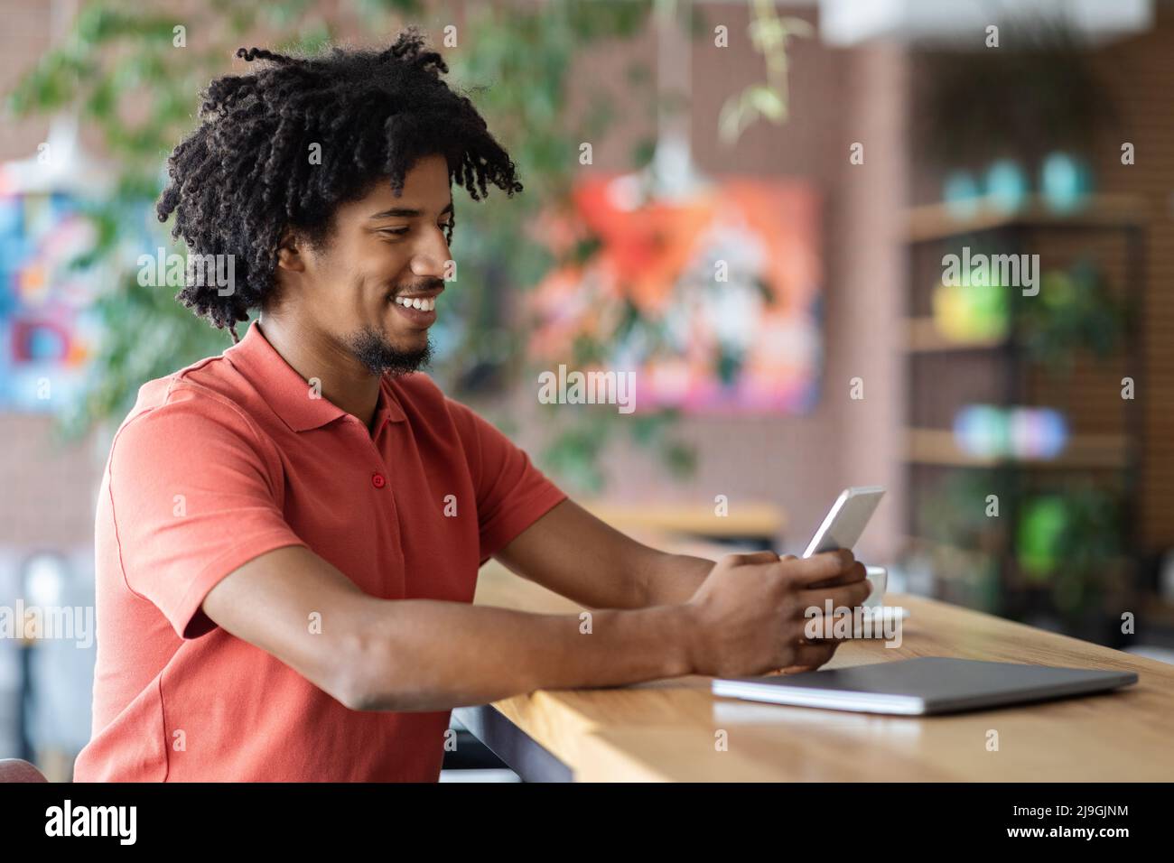 Cheerful curly handsome young black guy typing on smartphone, chatting ...