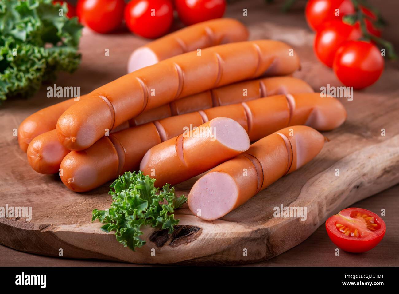 Grilled Frankfurter sausages styled on wooden board with tomotoes and ...