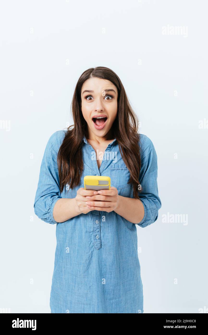 Surprised young brunette woman holding smartphone joyfully squeals ...