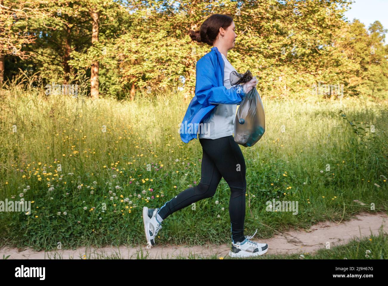 Young woman in sportswear jogging at the park and holding a bag of ...
