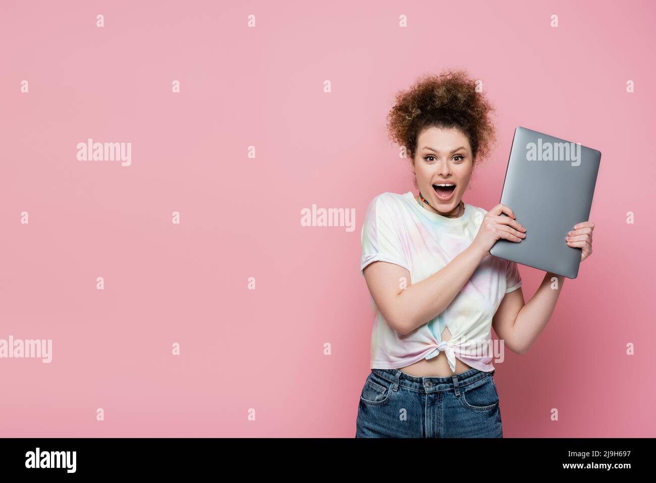 Amazed curly woman holding laptop isolated on pink Stock Photo - Alamy