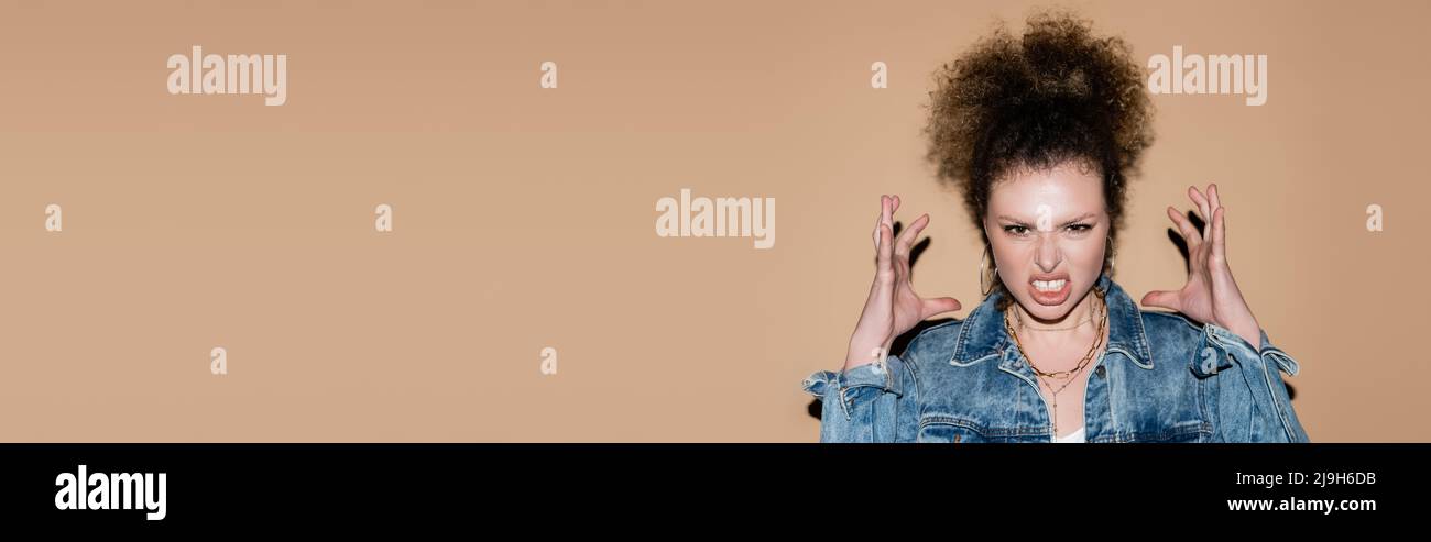 Aggressive model in denim jacket looking at camera on beige background ...