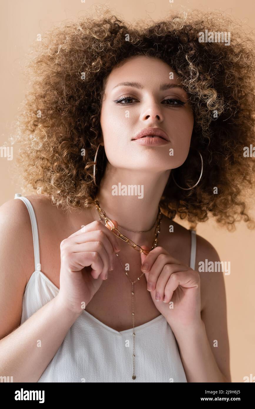 Pretty curly model touching necklace isolated on beige Stock Photo - Alamy