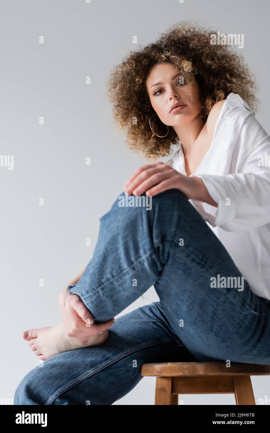 Low angle view of barefoot model sitting on chair isolated on white ...