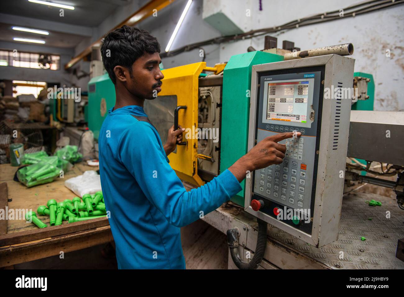 A worker operates an automatic molding machine at a plastic product ...