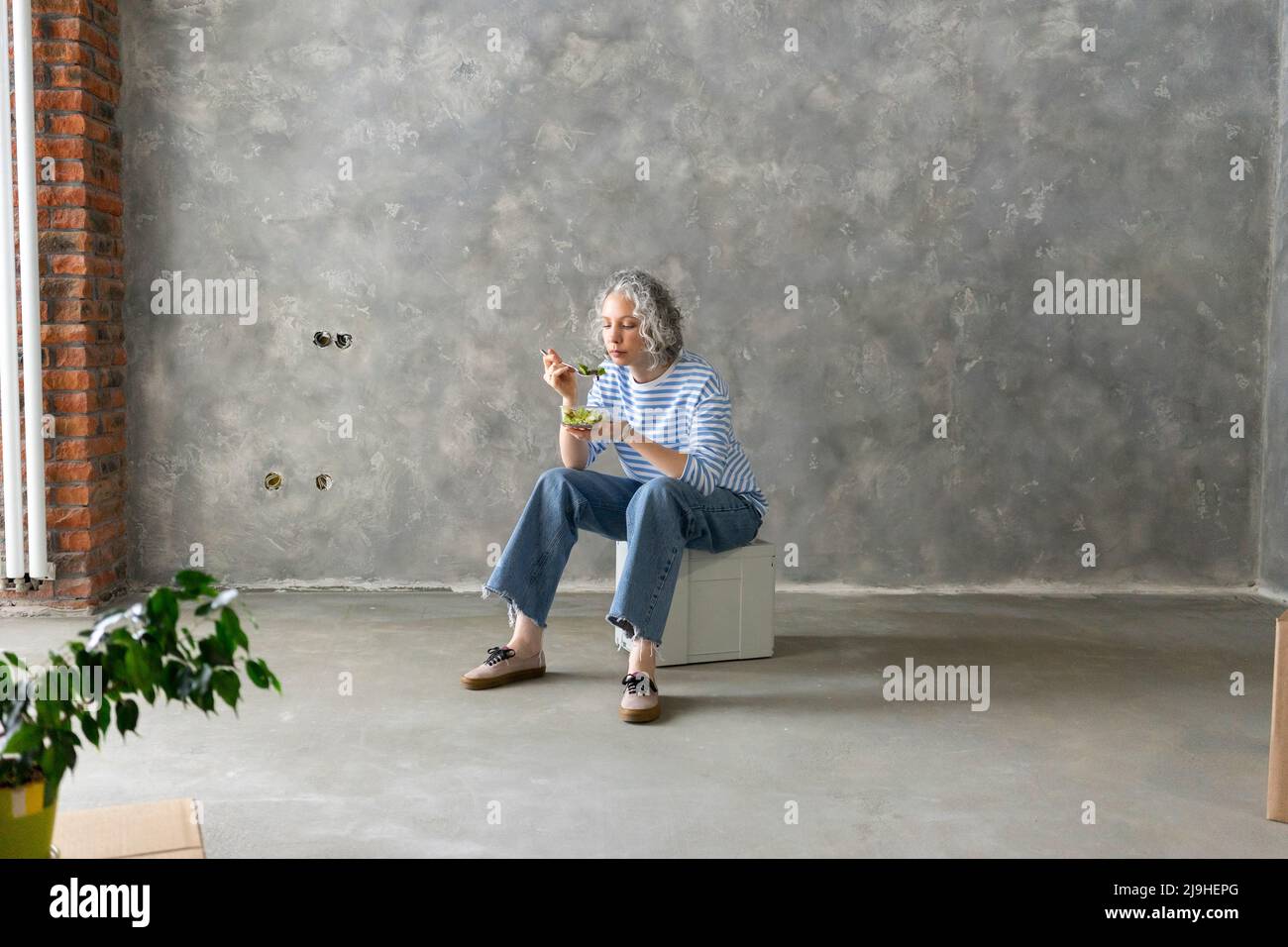 Woman eating lunch sitting on box in front of wall Stock Photo - Alamy