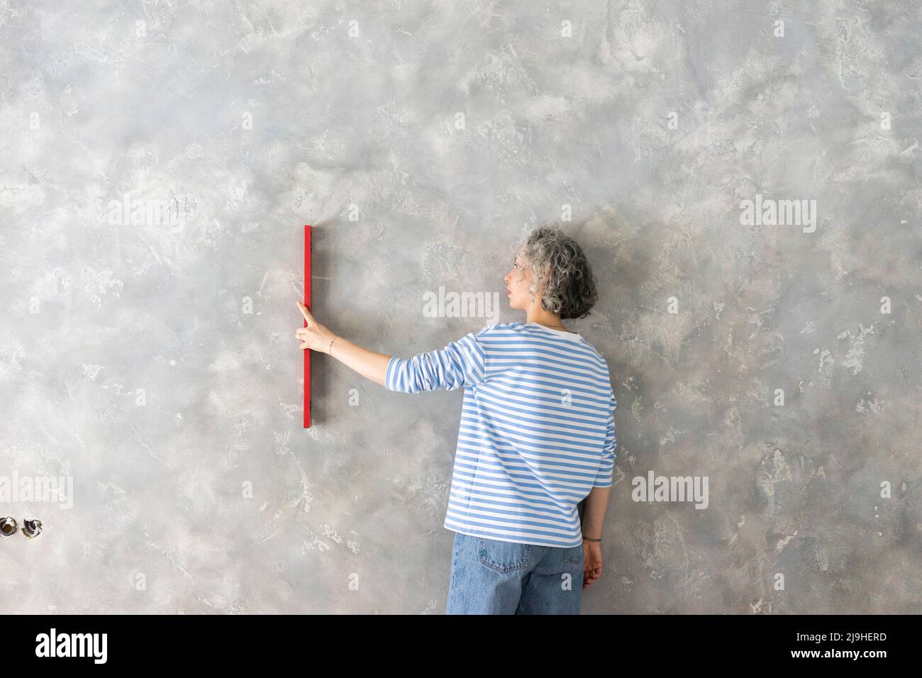 Woman with level measuring tool working on gray wall Stock Photo - Alamy
