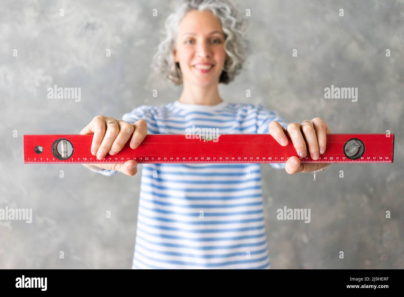 Smiling woman with level measuring tool in front of wall Stock Photo ...