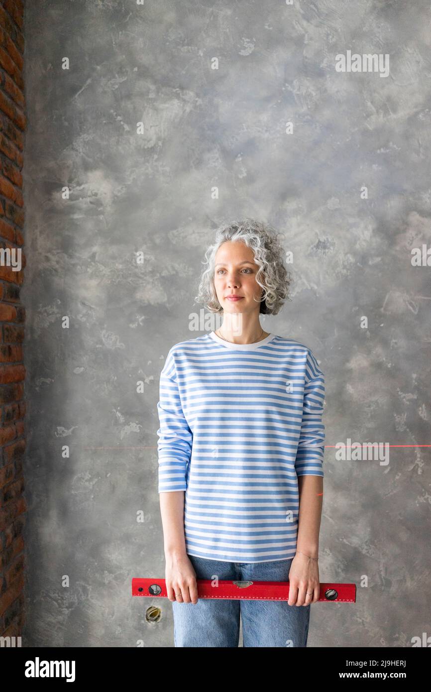 Woman with level measuring tool standing in front of gray wall Stock ...