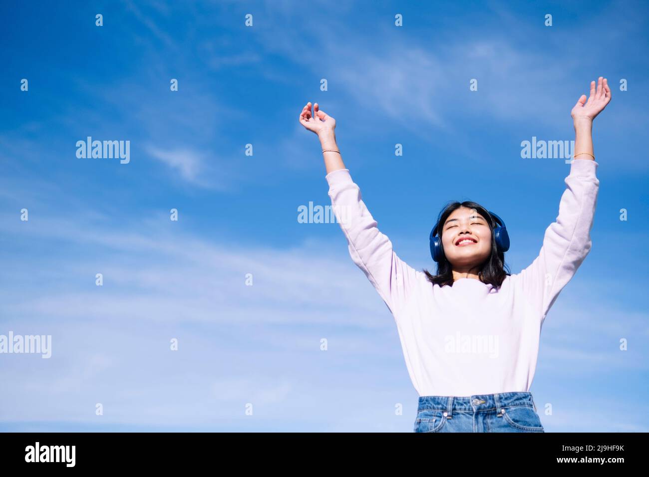 Happy woman listening music with hands raised in front of sky Stock ...