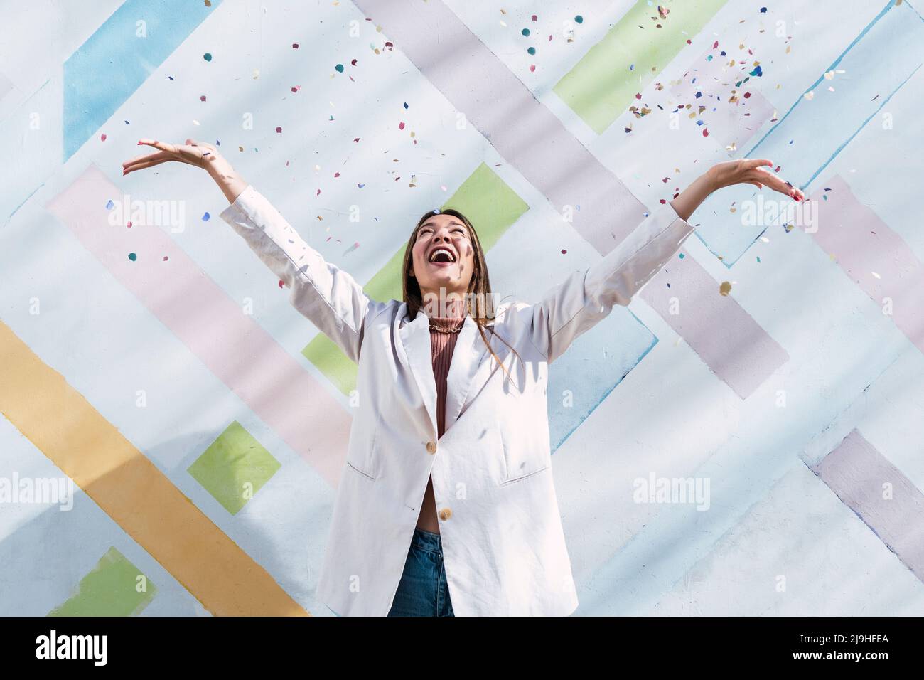 Happy woman throwing confetti standing in front of wall Stock Photo - Alamy