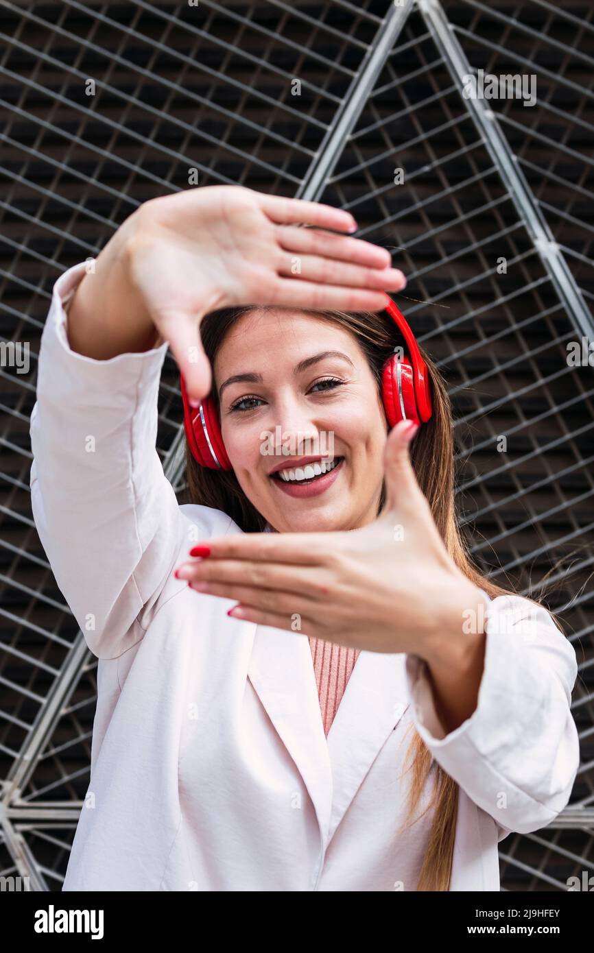 Happy woman gesturing finger frame standing in front of metal wall ...
