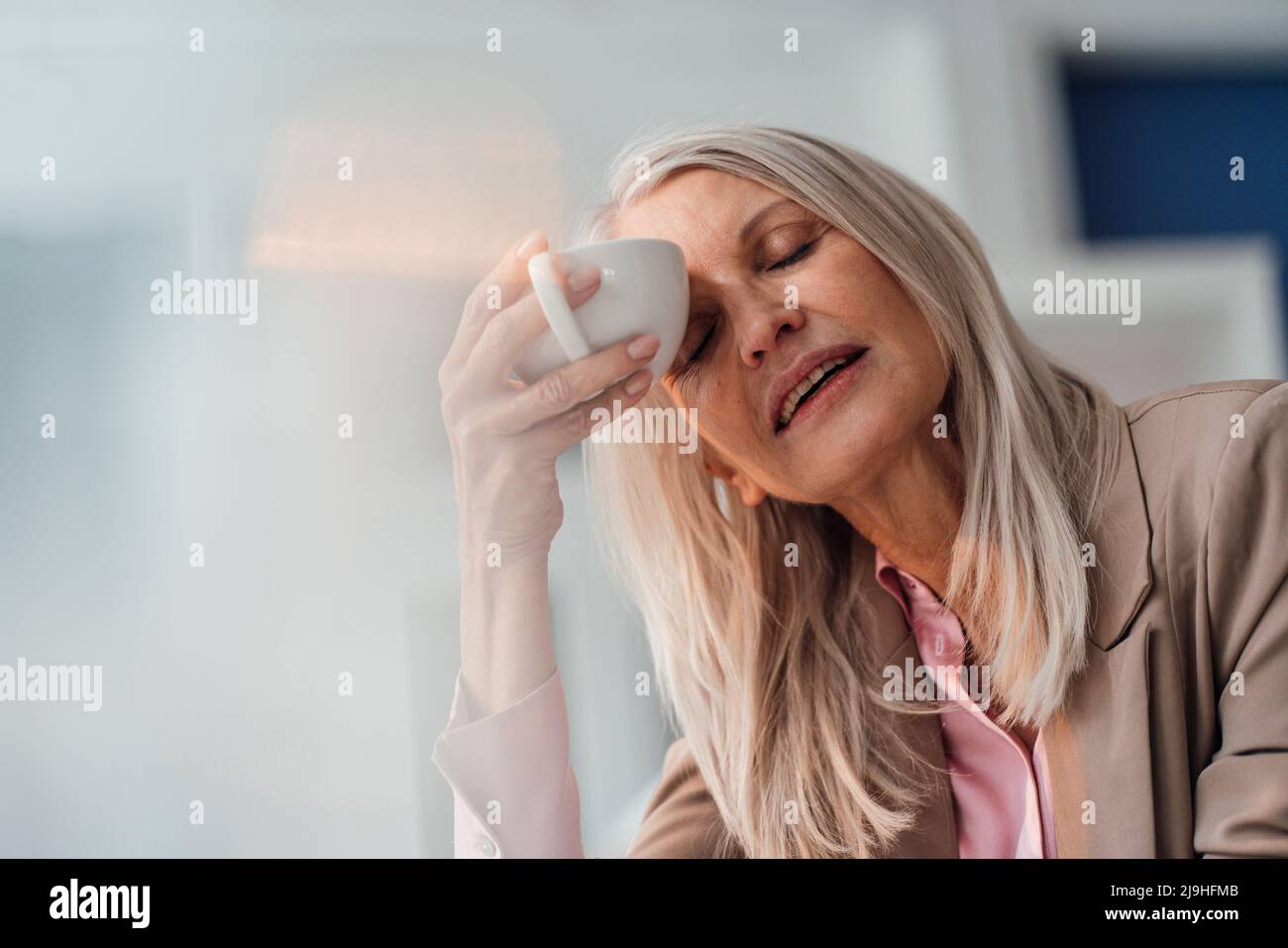 Tired businesswoman touching coffee cup on forehead at office Stock ...
