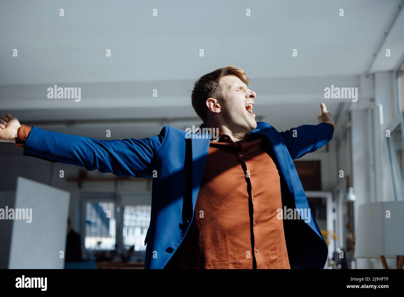 Businessman with arms outstretched yawning in office Stock Photo - Alamy