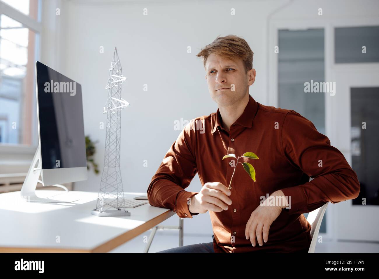 Thoughtful engineer holding leaf sitting by electricity pylon model at ...