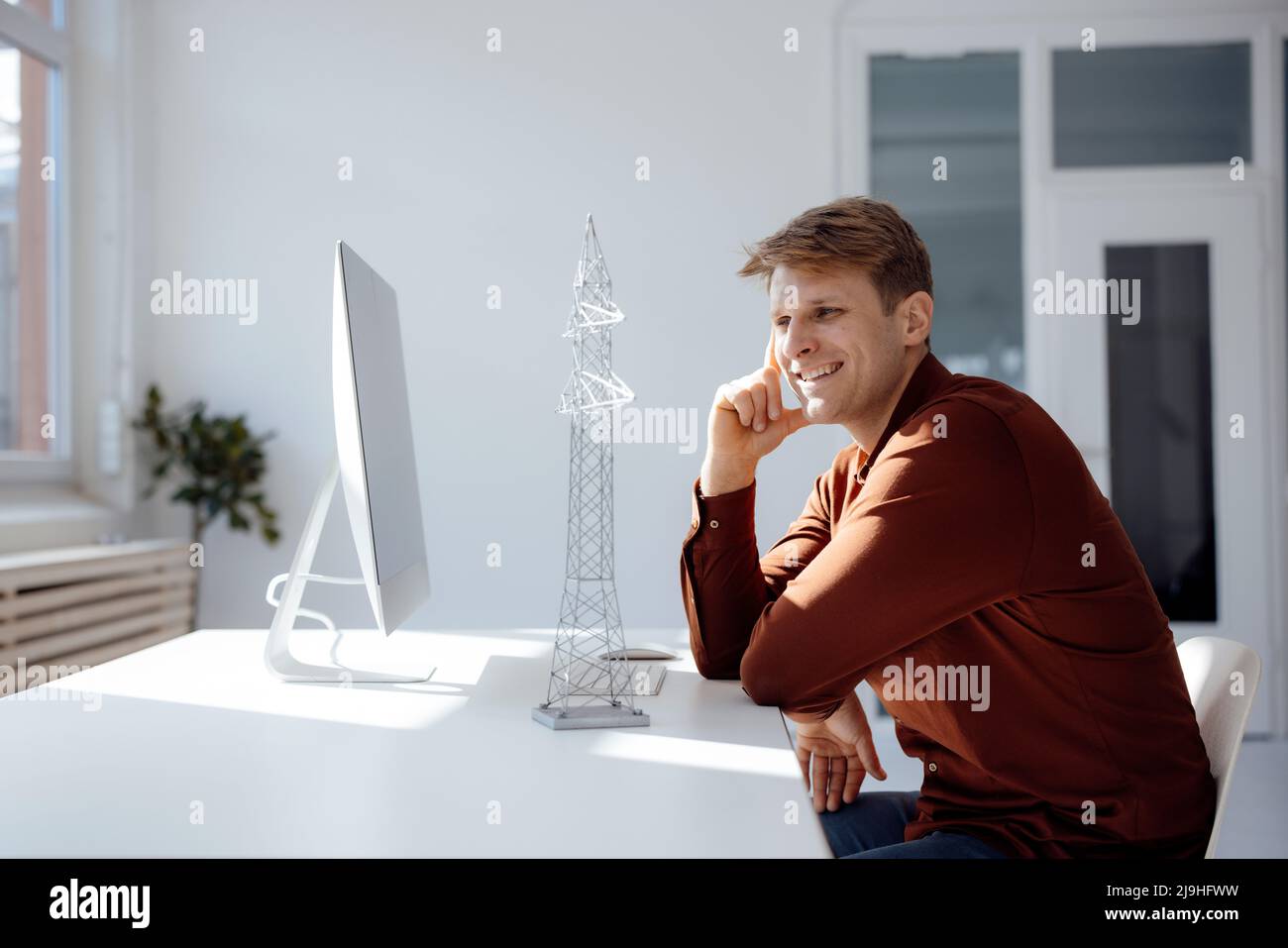 Happy engineer looking at electricity pylon model at desk in office ...