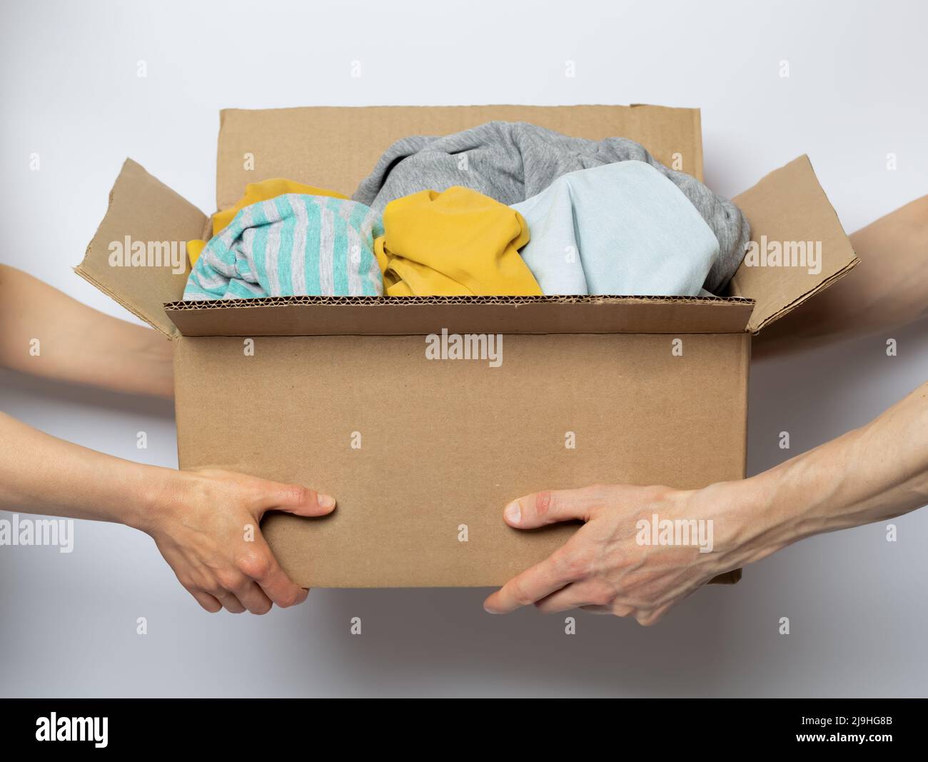 Hands give a donation or charity box with clothes on a white background ...