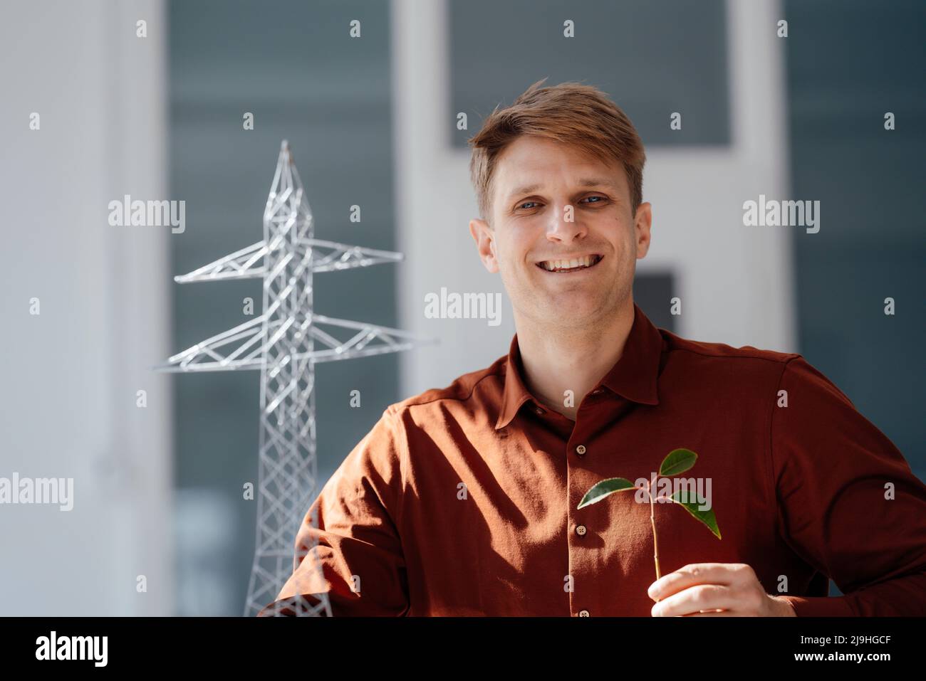 Happy engineer holding leaf sitting by electricity pylon model at desk ...