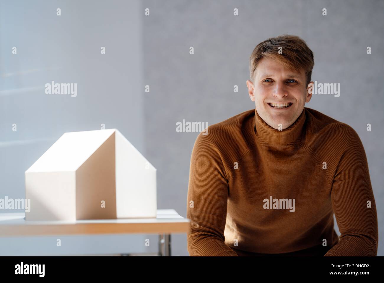 Happy architect sitting by model house in office Stock Photo - Alamy