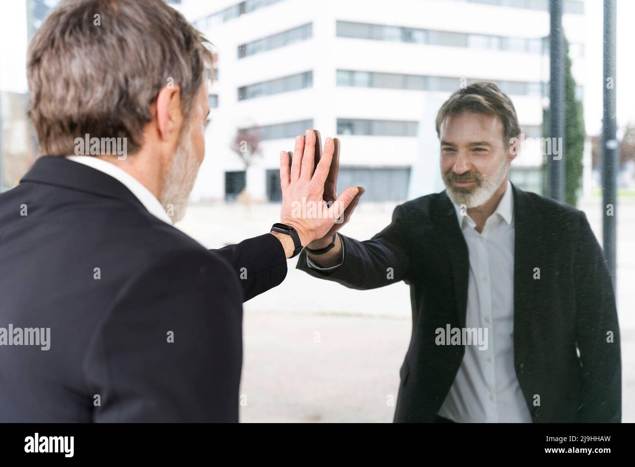 Businessman touching reflection on glass wall Stock Photo - Alamy