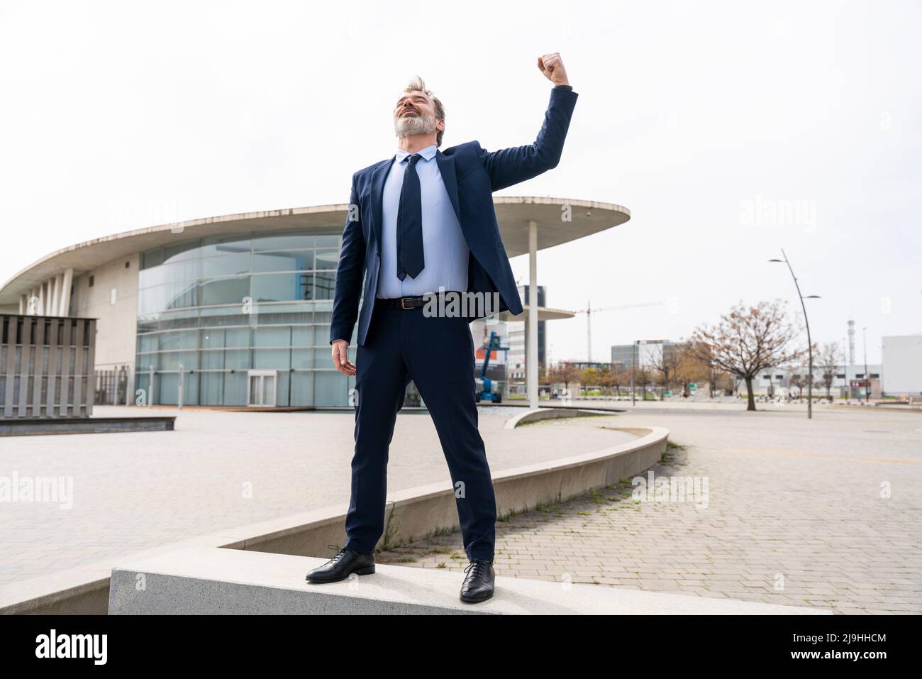 Businessman flexing muscles standing on wall at office park Stock Photo ...