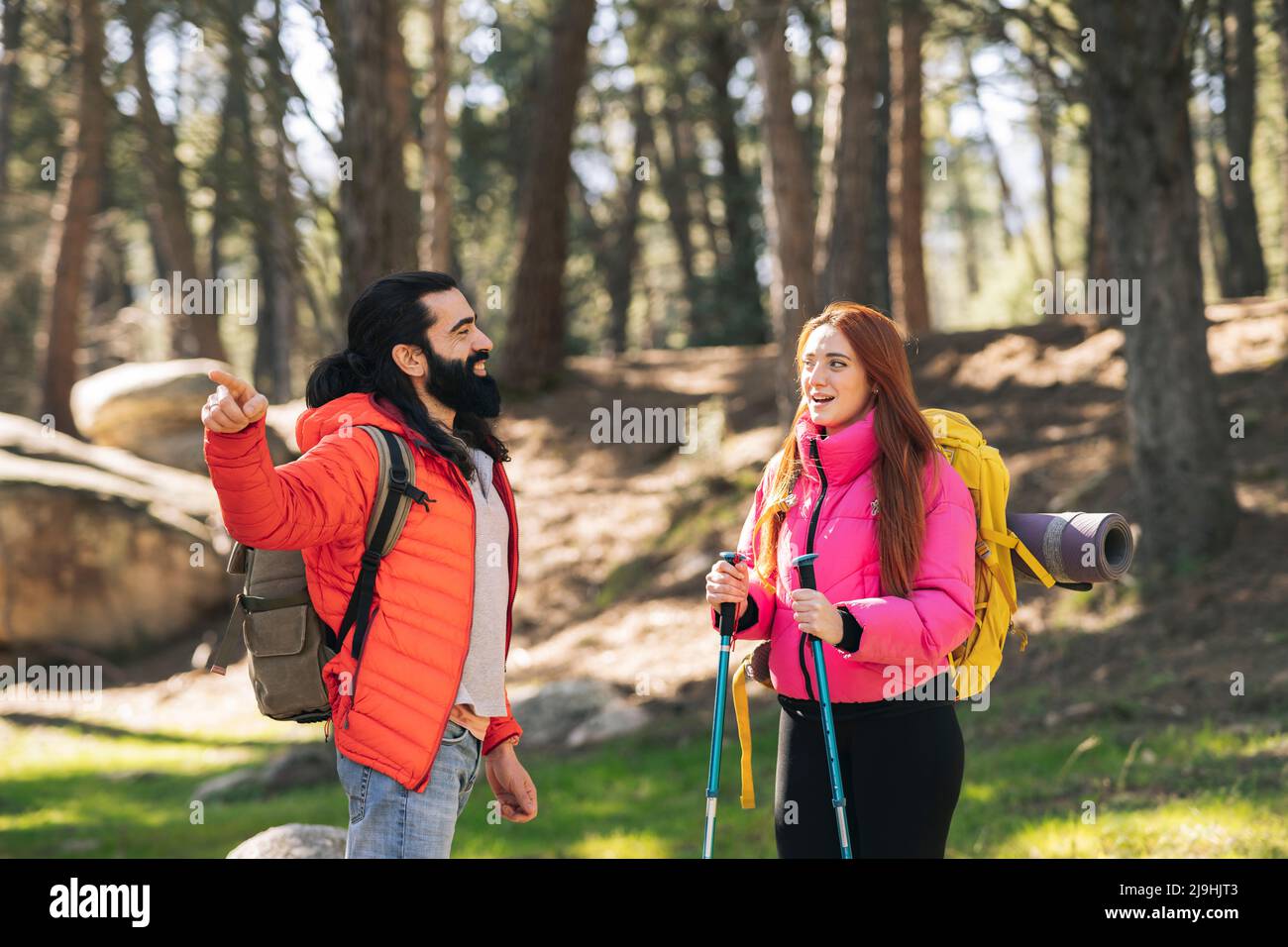 Young woman talking with boyfriend wearing backpack pointing in forest ...