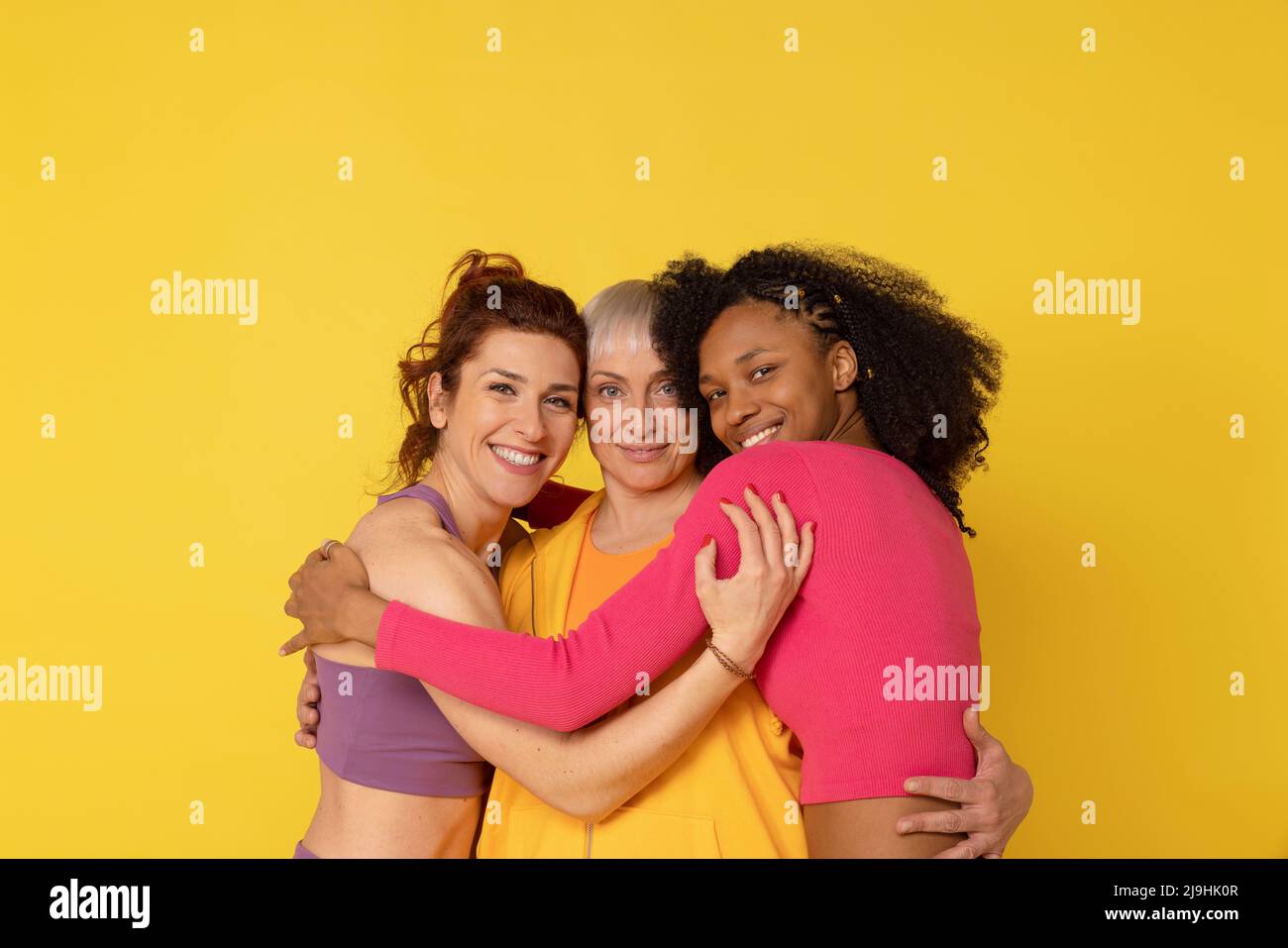 Smiling multiracial friends hugging each other against yellow ...