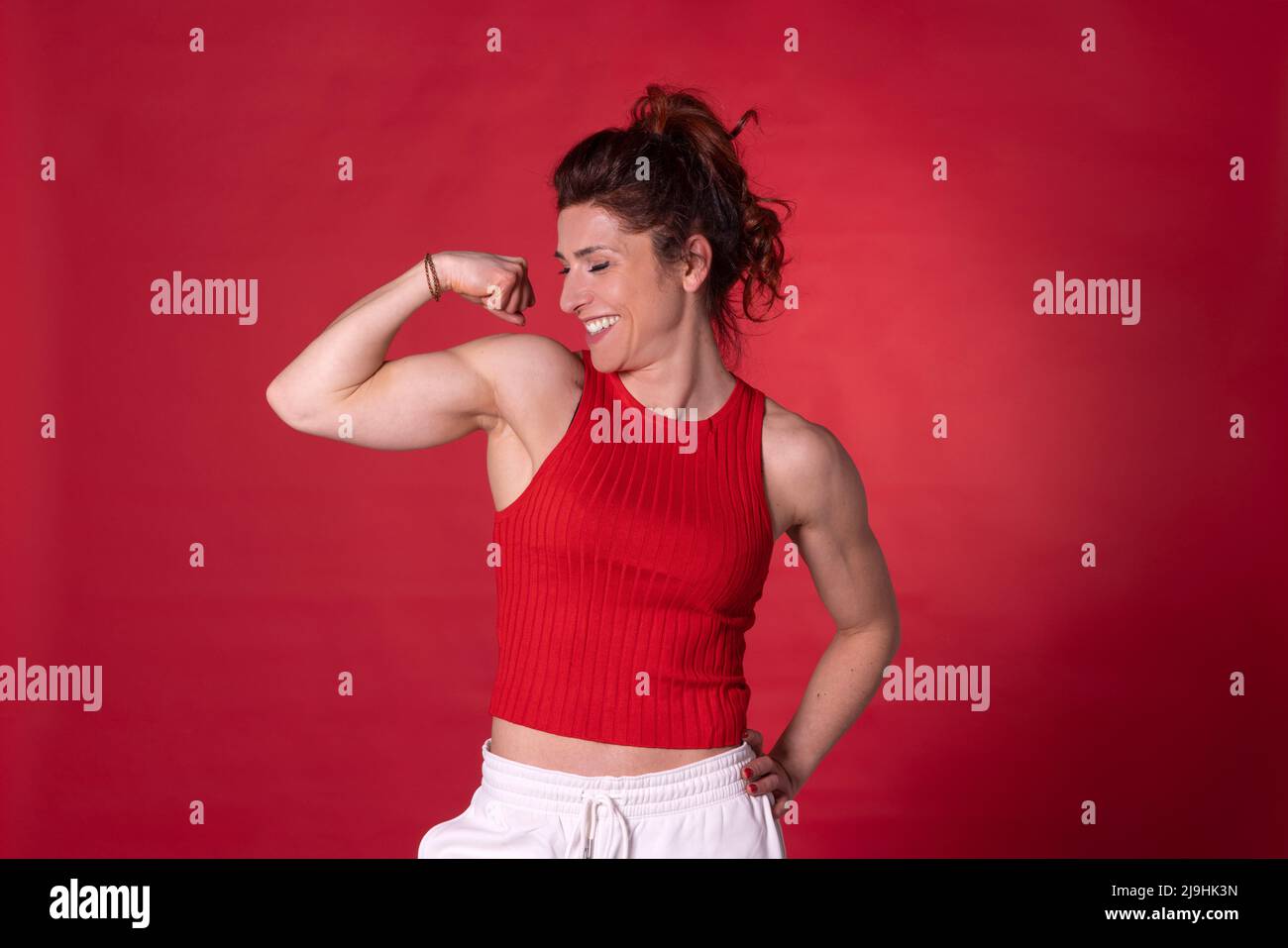 Smiling woman flexing muscles against red background Stock Photo - Alamy