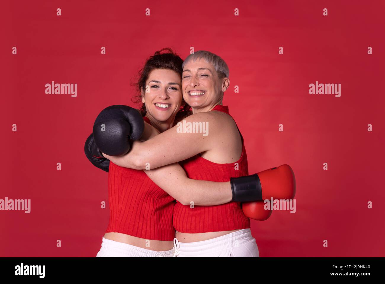 Smiling friends wearing boxing gloves hugging each other against red ...