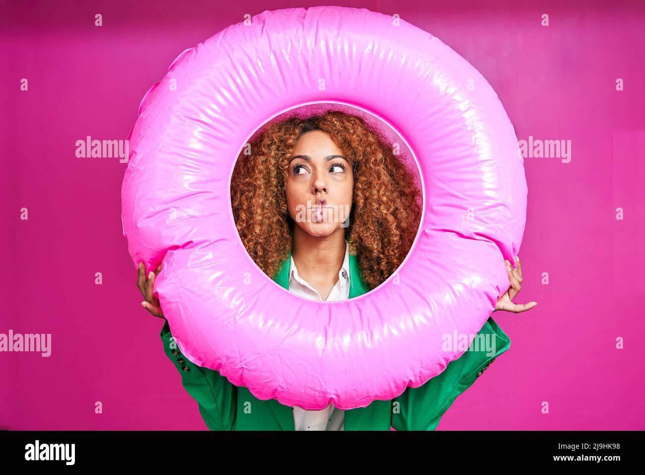 Businesswoman making face looking though inflatable ring against pink ...