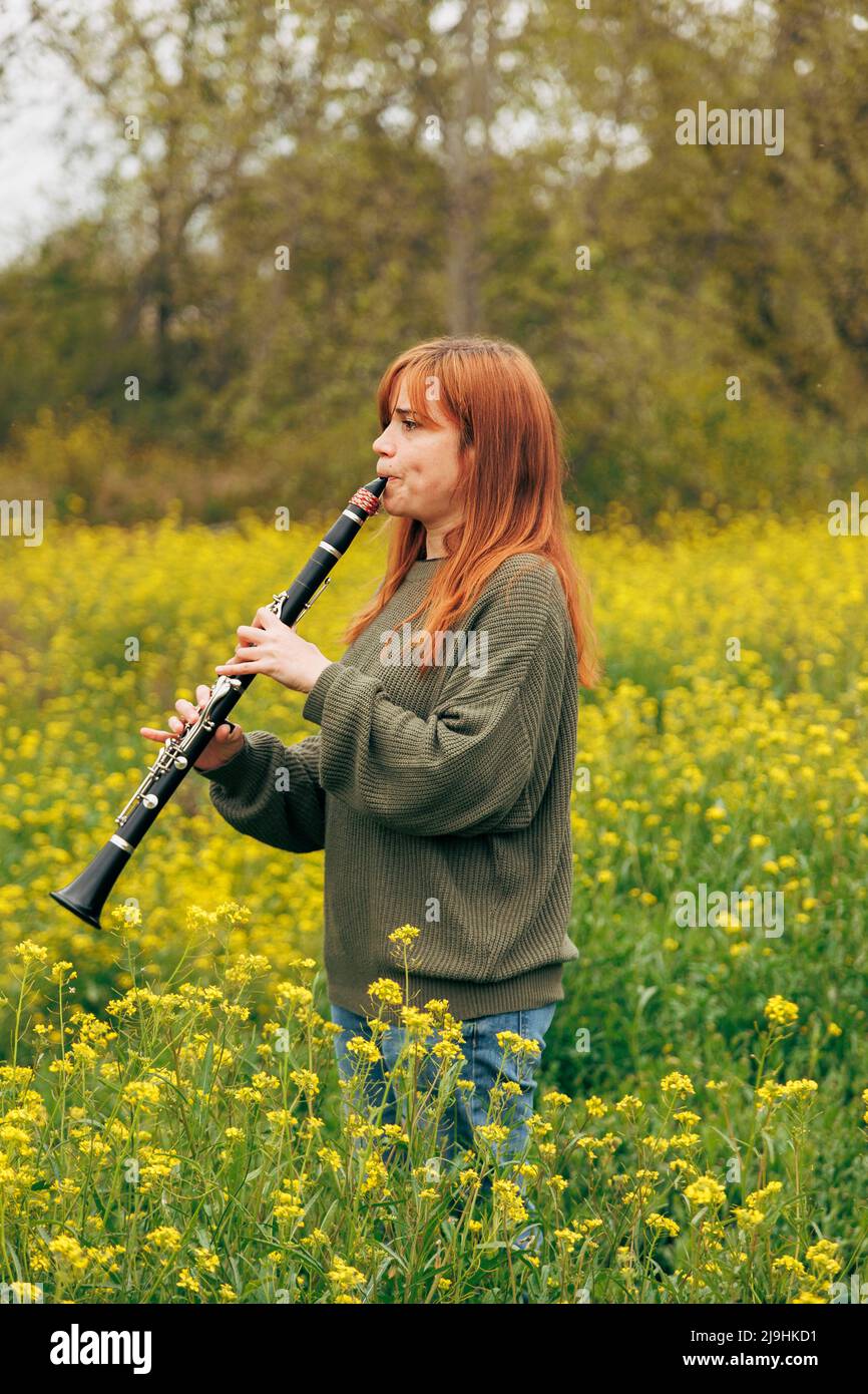 Redhead woman practicing clarinet standing in flower field Stock Photo ...
