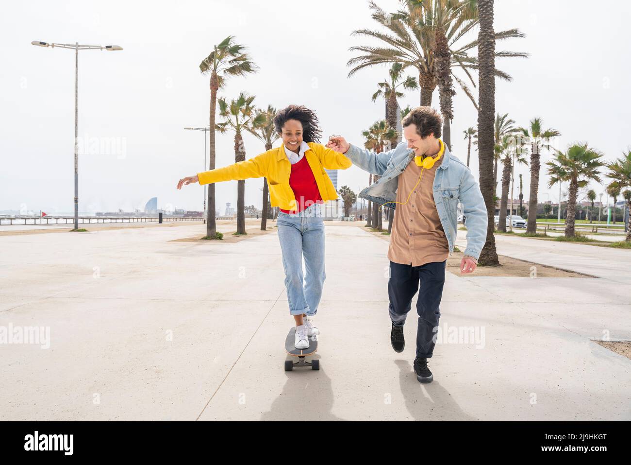 Happy man teaching skateboarding to woman on footpath Stock Photo - Alamy