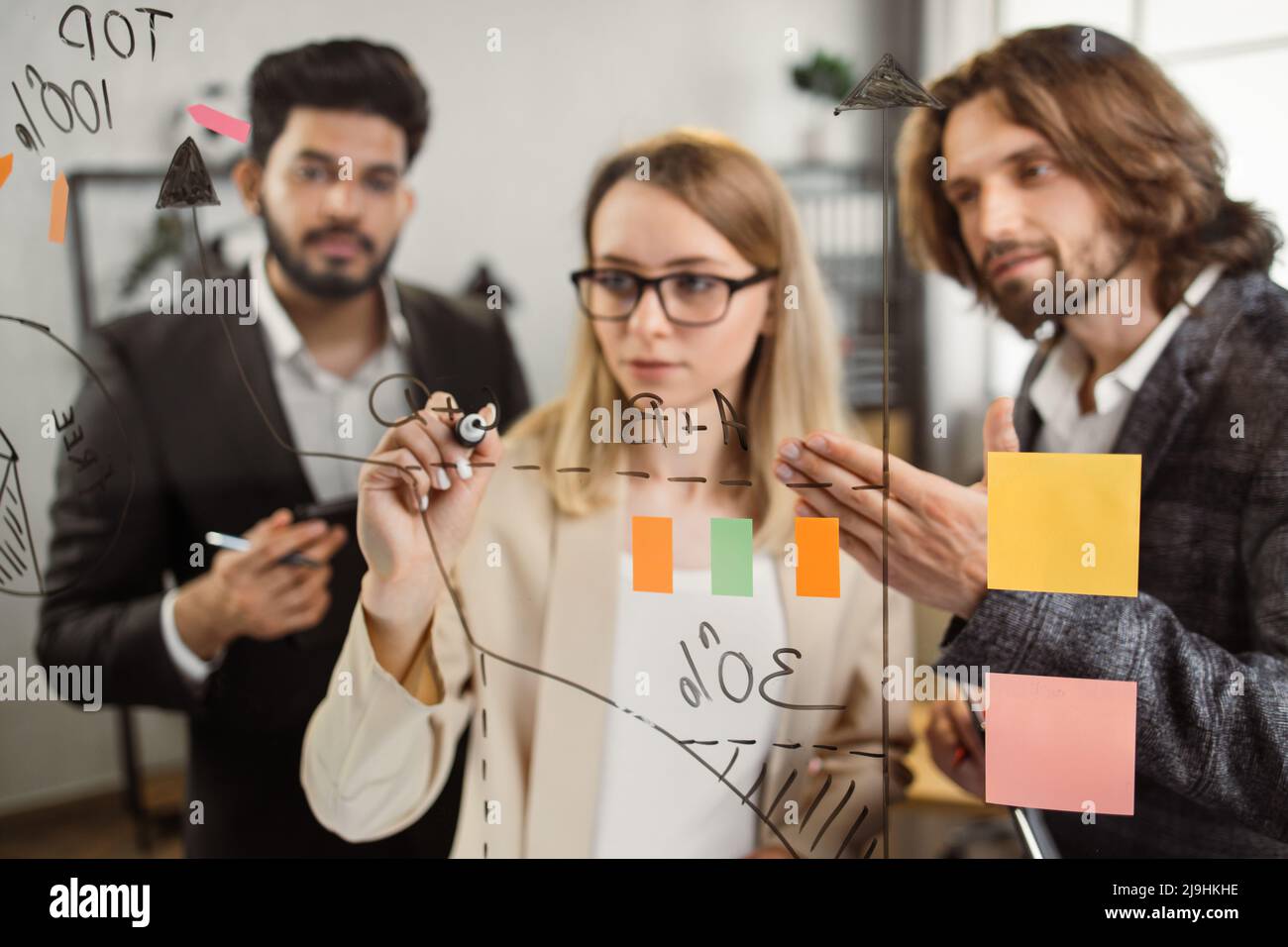 Female analyst in formal wear presenting strategy graphs on glass board ...