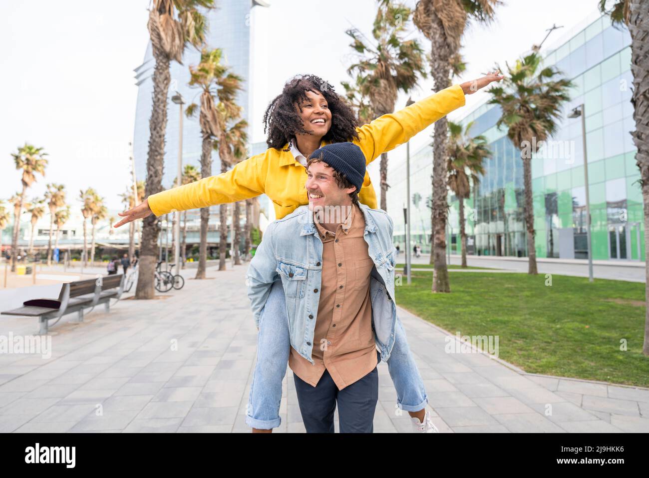 Happy woman with arms outstretched enjoying piggyback ride with man on ...