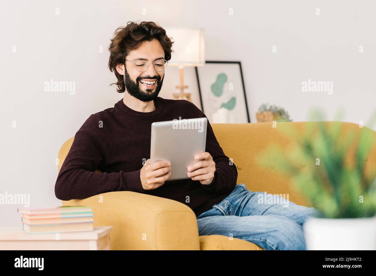 Happy man on video call through tablet PC sitting in living room at ...