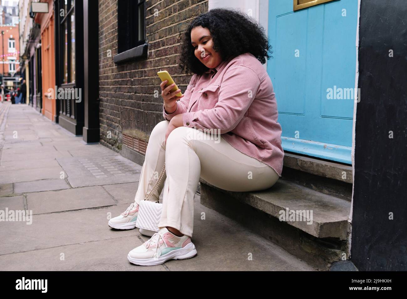 Smiling woman text messaging through smart phone sitting on step Stock ...