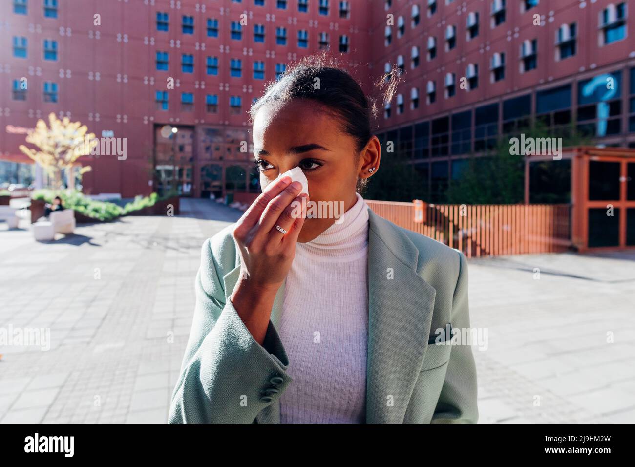 Sad businesswoman wiping tears with tissue in front of office building ...