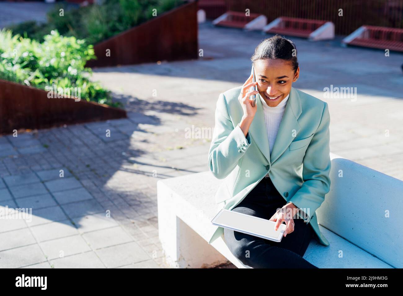 Smiling freelancer talking over smart phone sitting on bench Stock ...