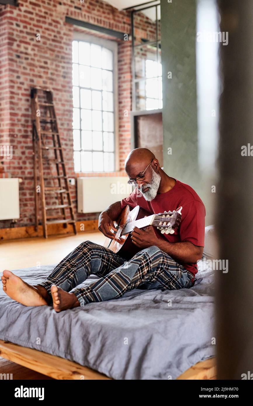 Mature man playing instrument on bed in bedroom Stock Photo - Alamy