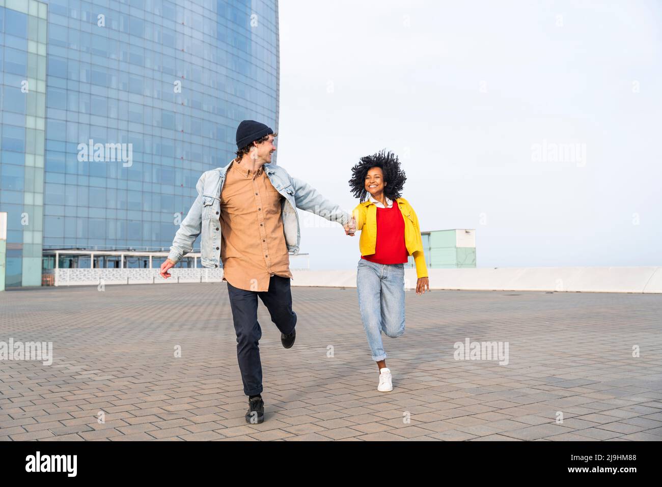 Happy Couple Holding Hands Running On Footpath In Front Of Building
