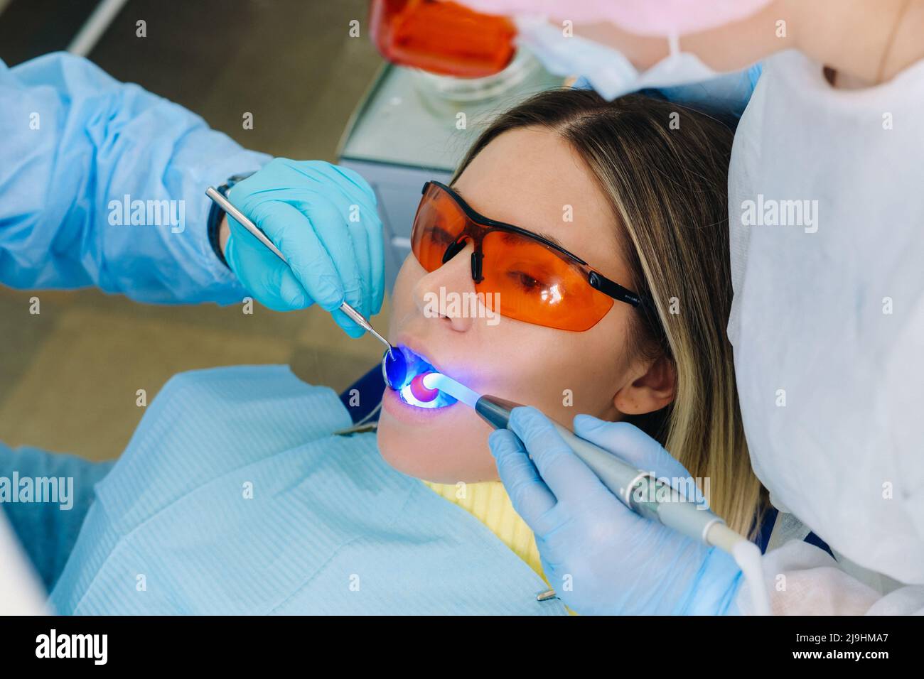 A young beautiful girl in dental glasses treats her teeth at the dentist with ultraviolet light ...