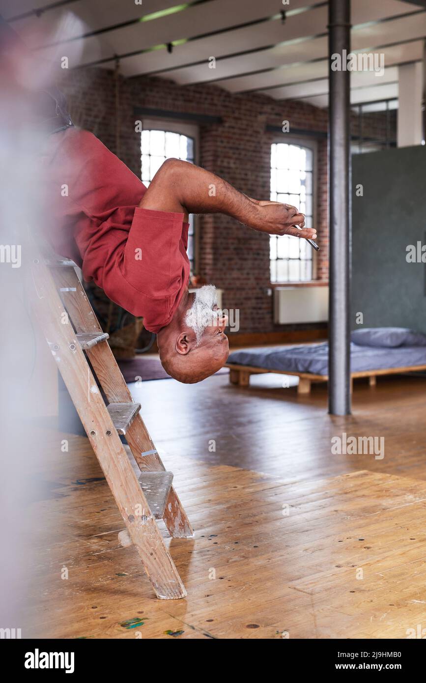 Man using mobile phone and bending backwards on ladder at home Stock ...