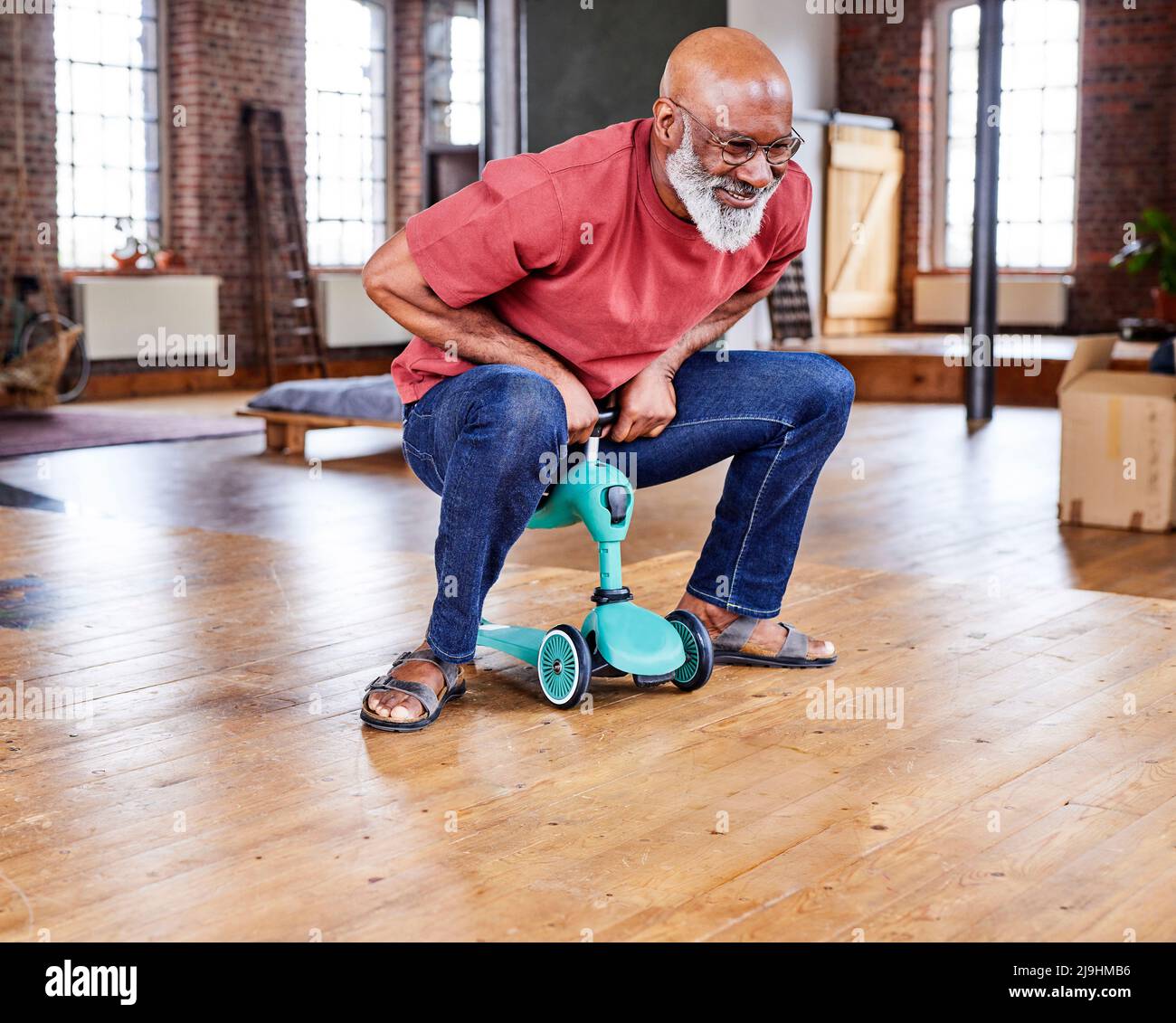 Smiling man riding small tricycle on floor at home Stock Photo - Alamy