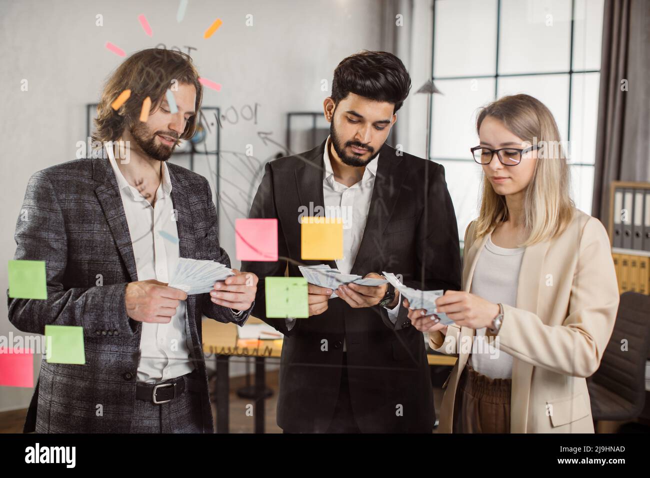 Confident multicultural investors counting money after profitable ...