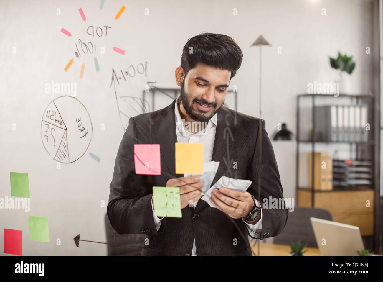 View through glass wall of young male manager in stylish formal suit ...