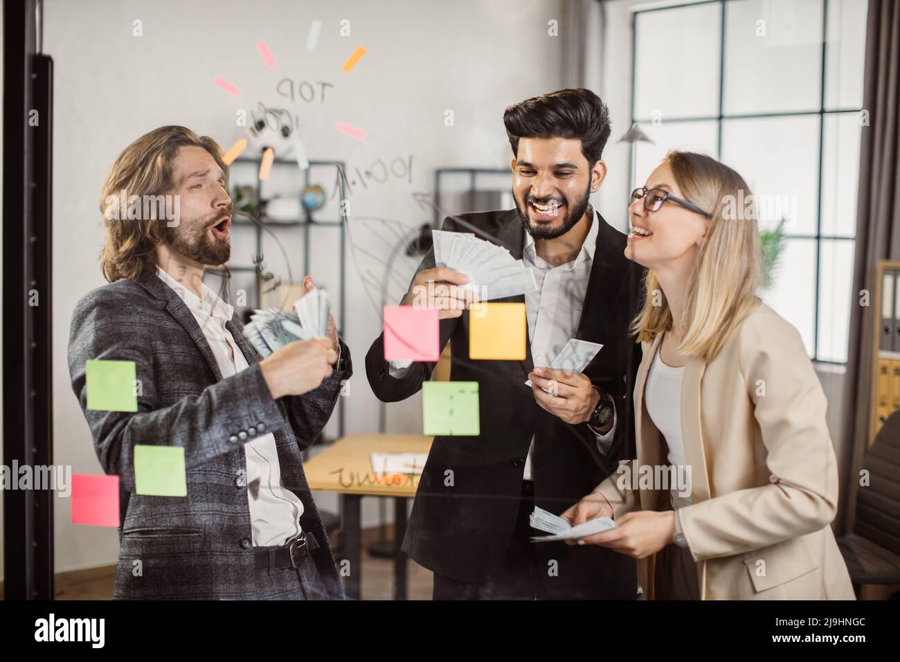 Joyful multietnic partners holding earned money cash while standing ...