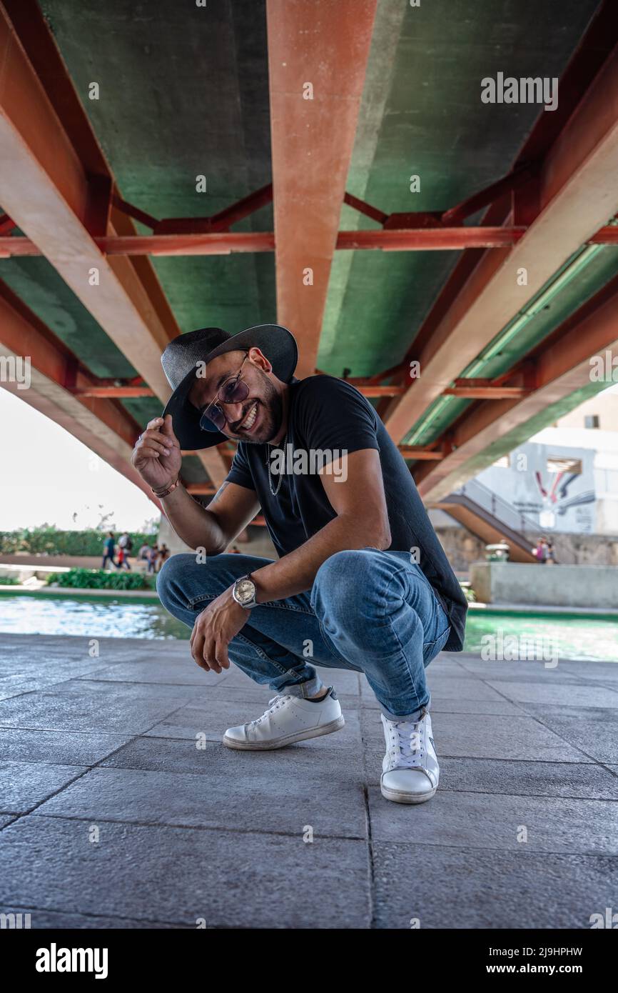 Young man smiling and posing under a bridge in a city with a river in ...