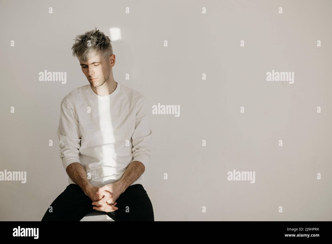 Stressed young man with hands clasped sitting on chair against white ...