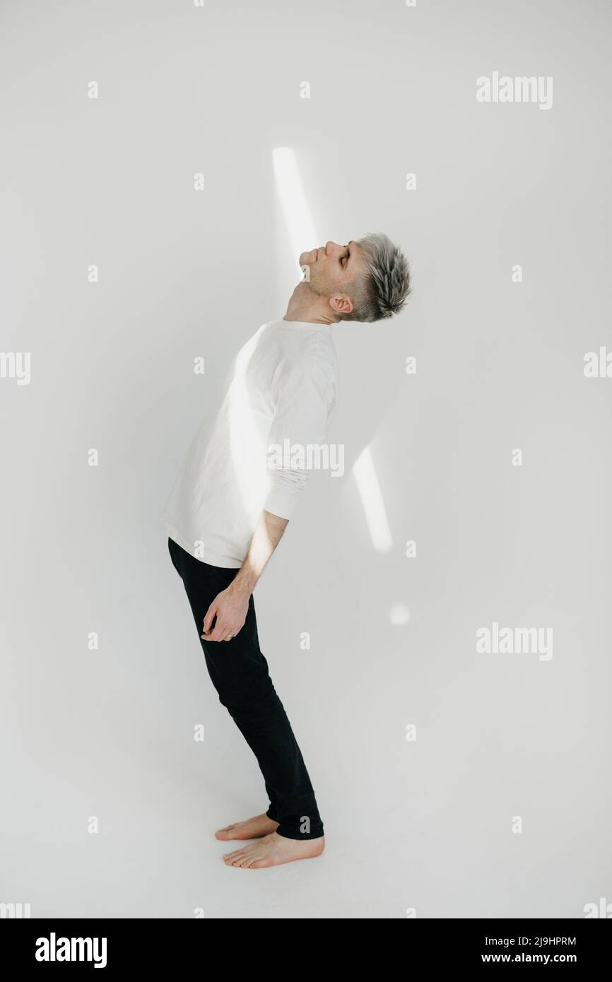 Young man with eyes closed bending backwards against white background ...